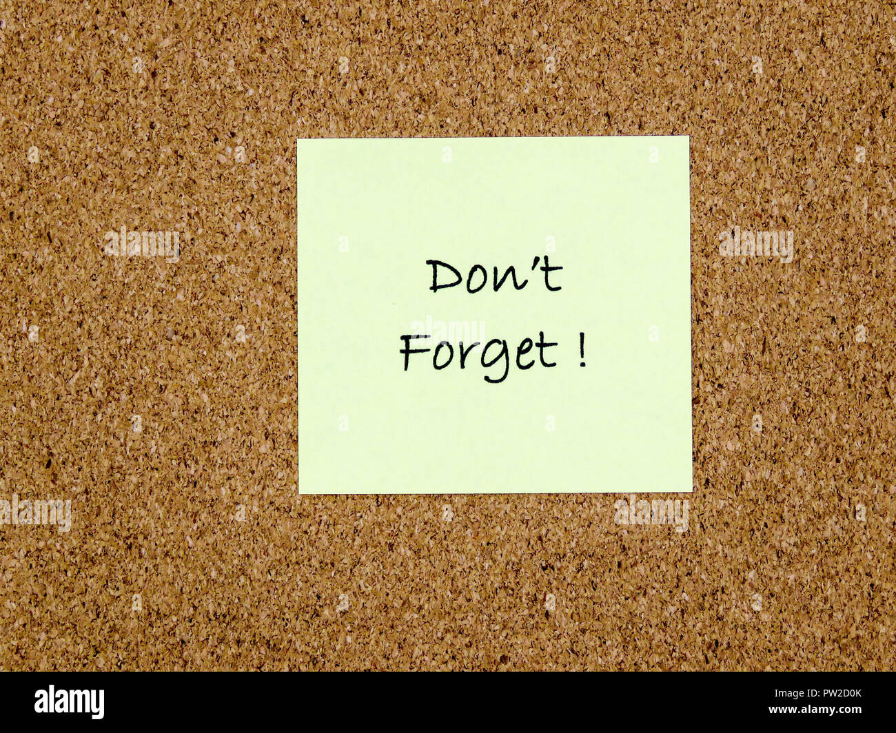 A yellow sticky note with don't forget written on it on a cork board ...