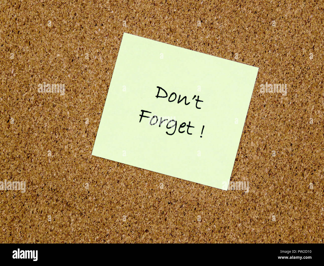 A yellow sticky note with don't forget written on it on a cork board ...