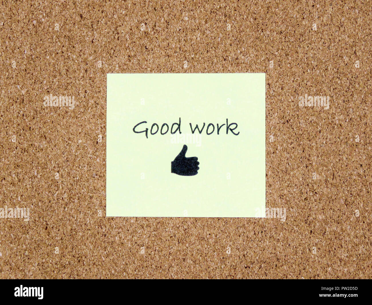 A yellow sticky note with good work written on it on a cork board ...