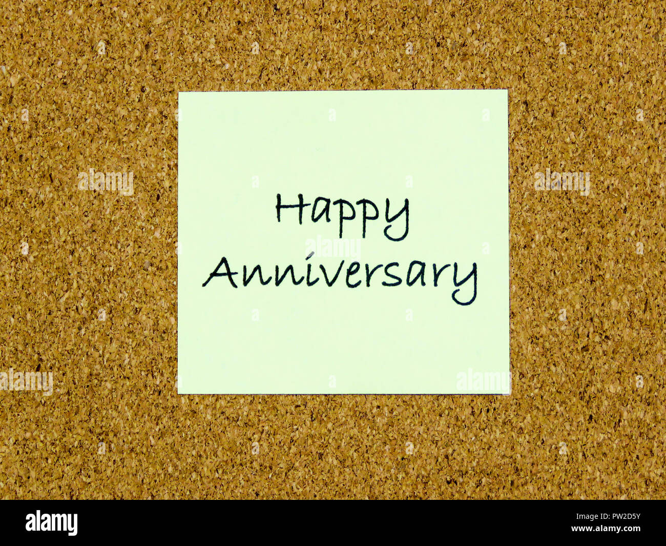 A yellow sticky note with happy anniversary written on it on a cork ...