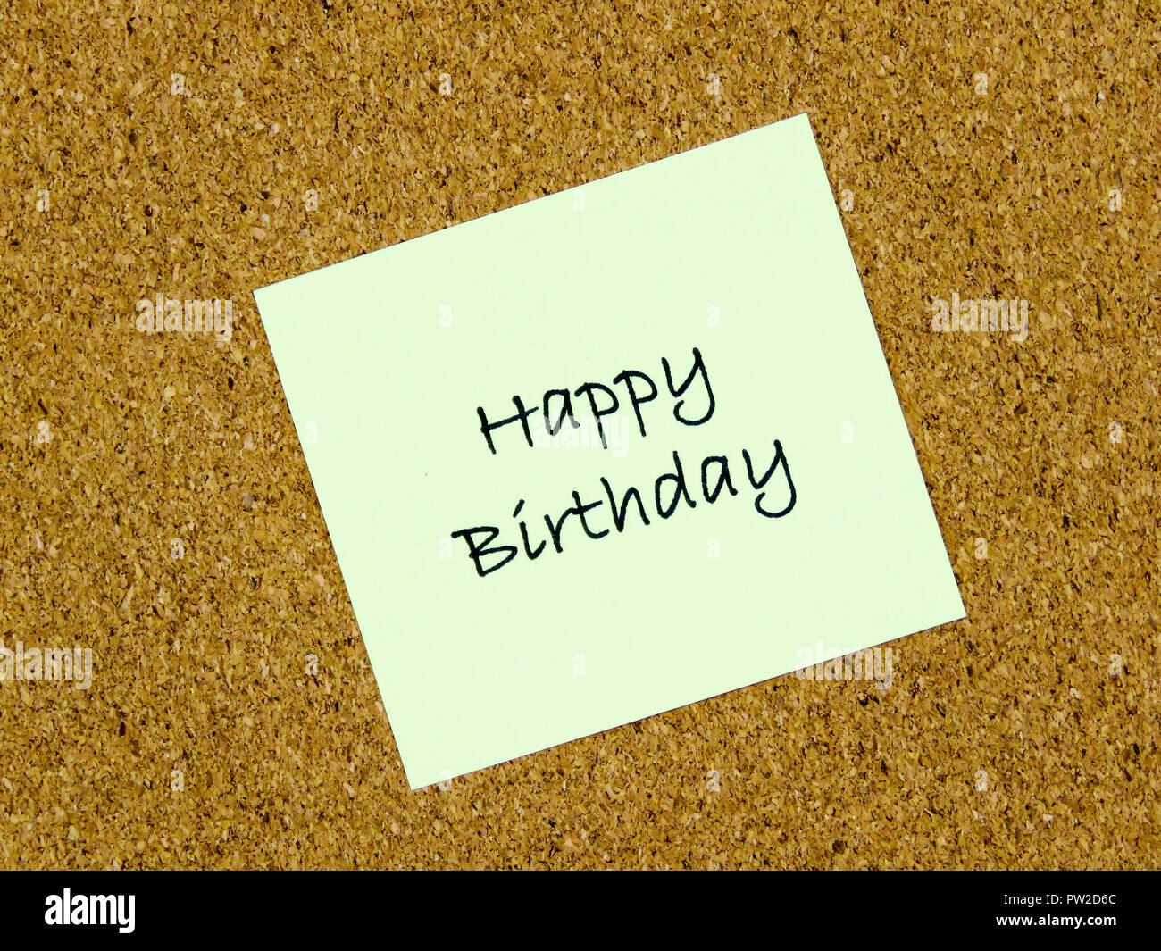 A yellow sticky note with happy birthday written on it on a cork board ...