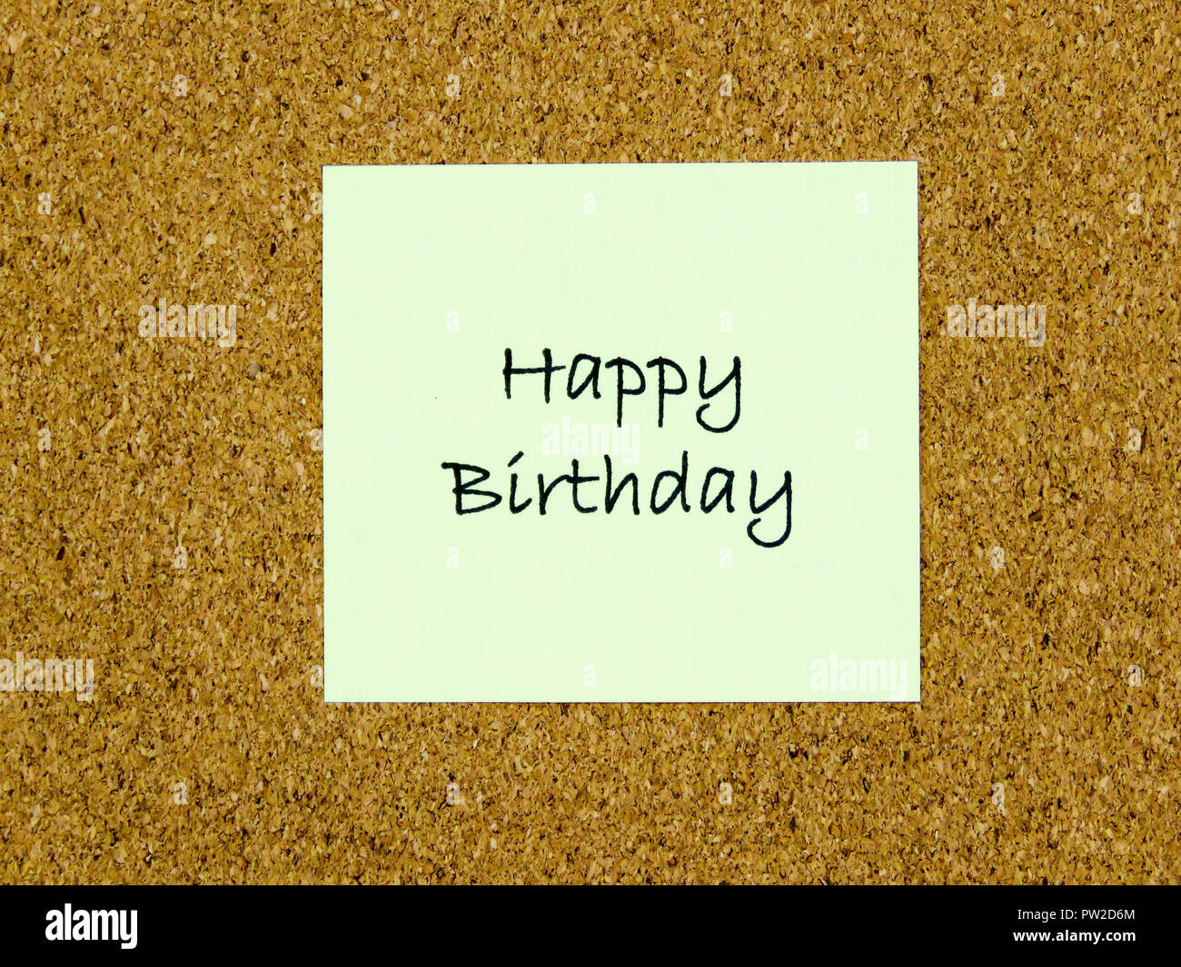 A yellow sticky note with happy birthday written on it on a cork board ...