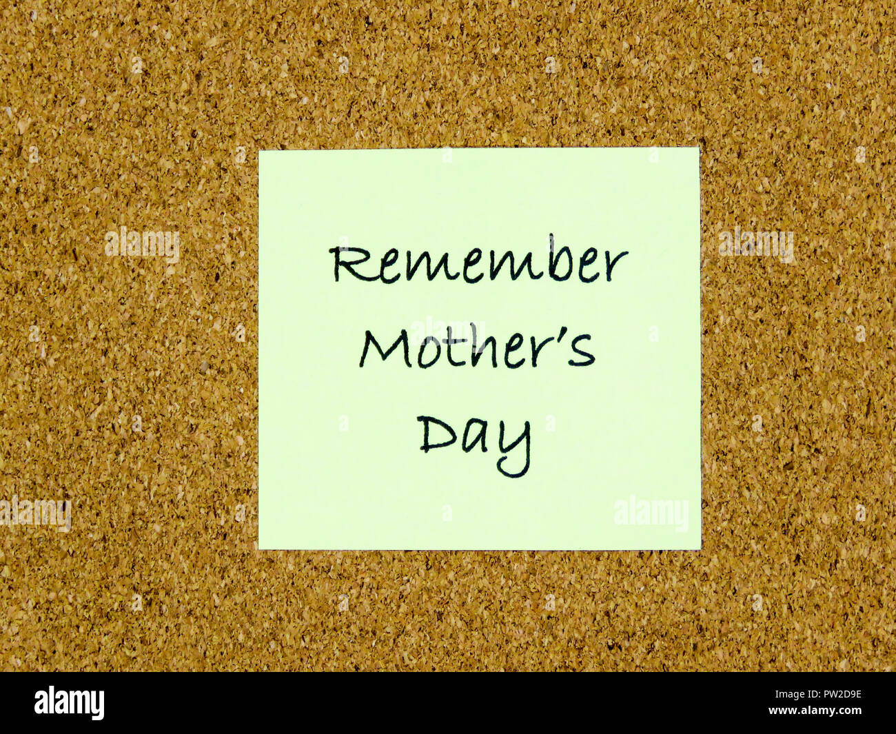 A yellow sticky note with mothers day written on it on a cork board ...