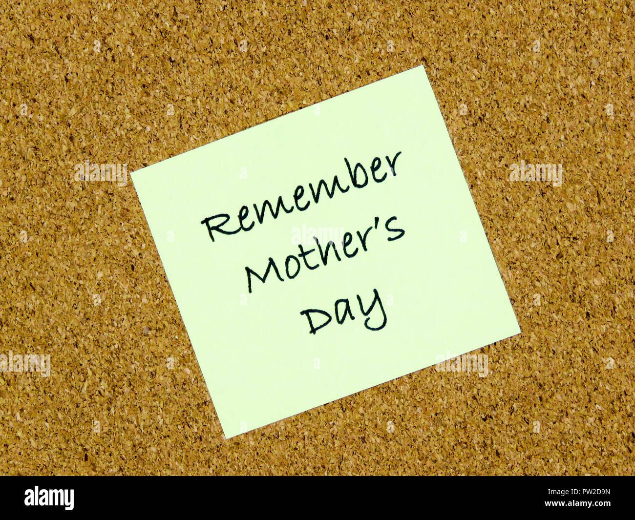 A yellow sticky note with mothers day written on it on a cork board ...