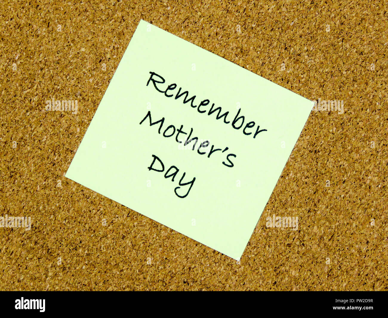A yellow sticky note with mothers day written on it on a cork board ...