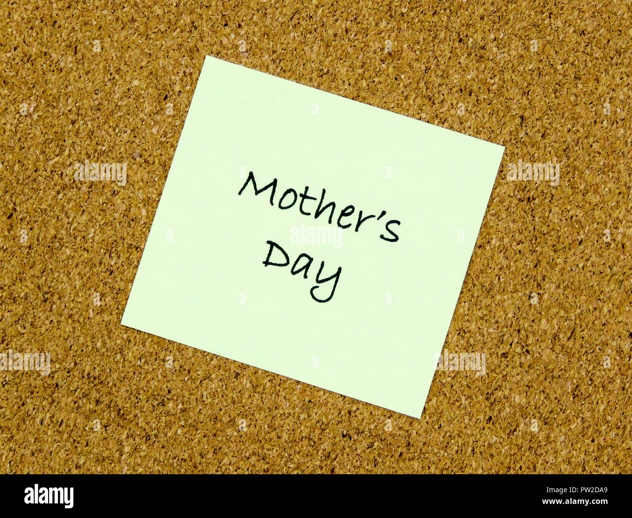 A yellow sticky note with mothers day written on it on a cork board ...