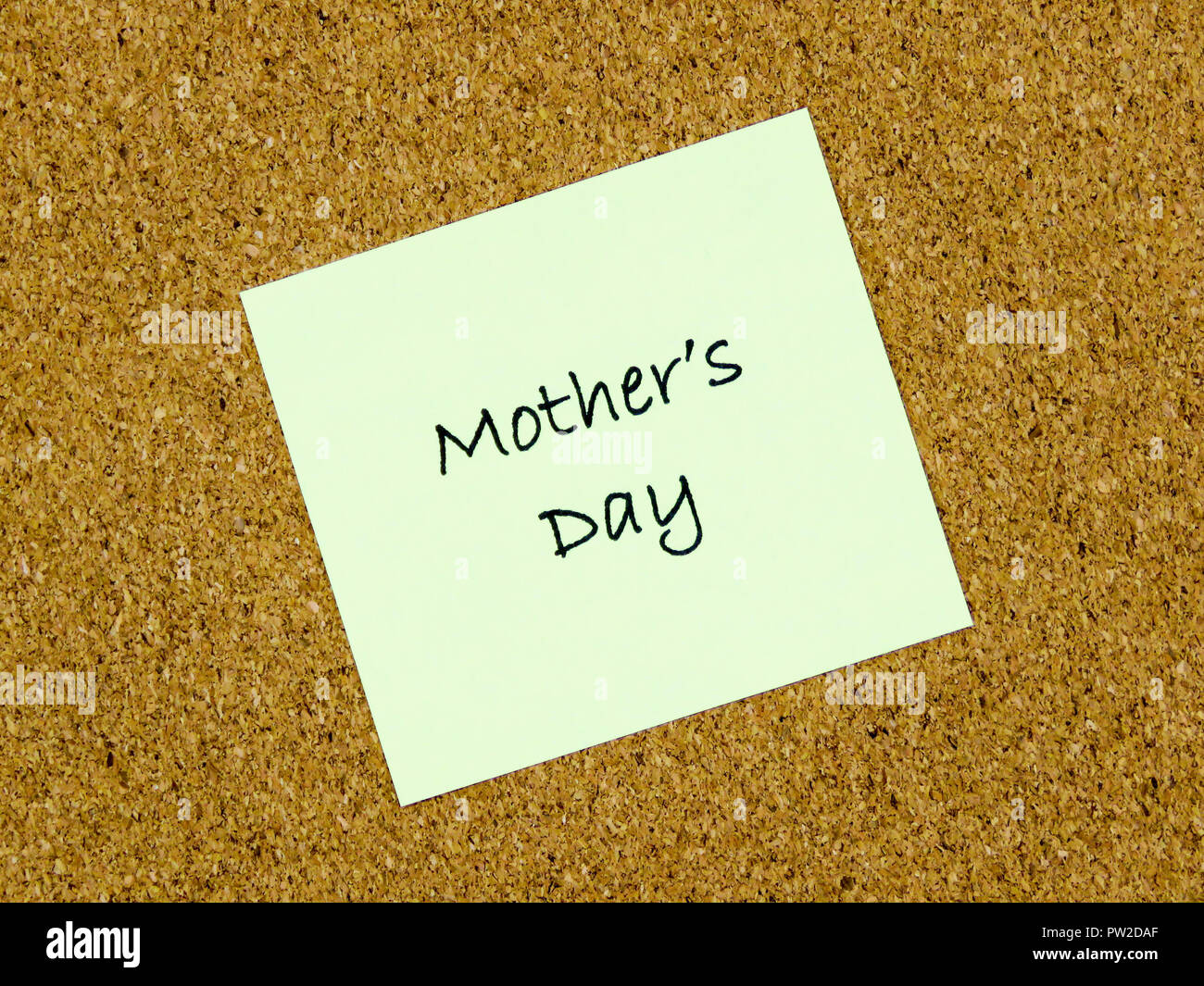 A yellow sticky note with mothers day written on it on a cork board ...