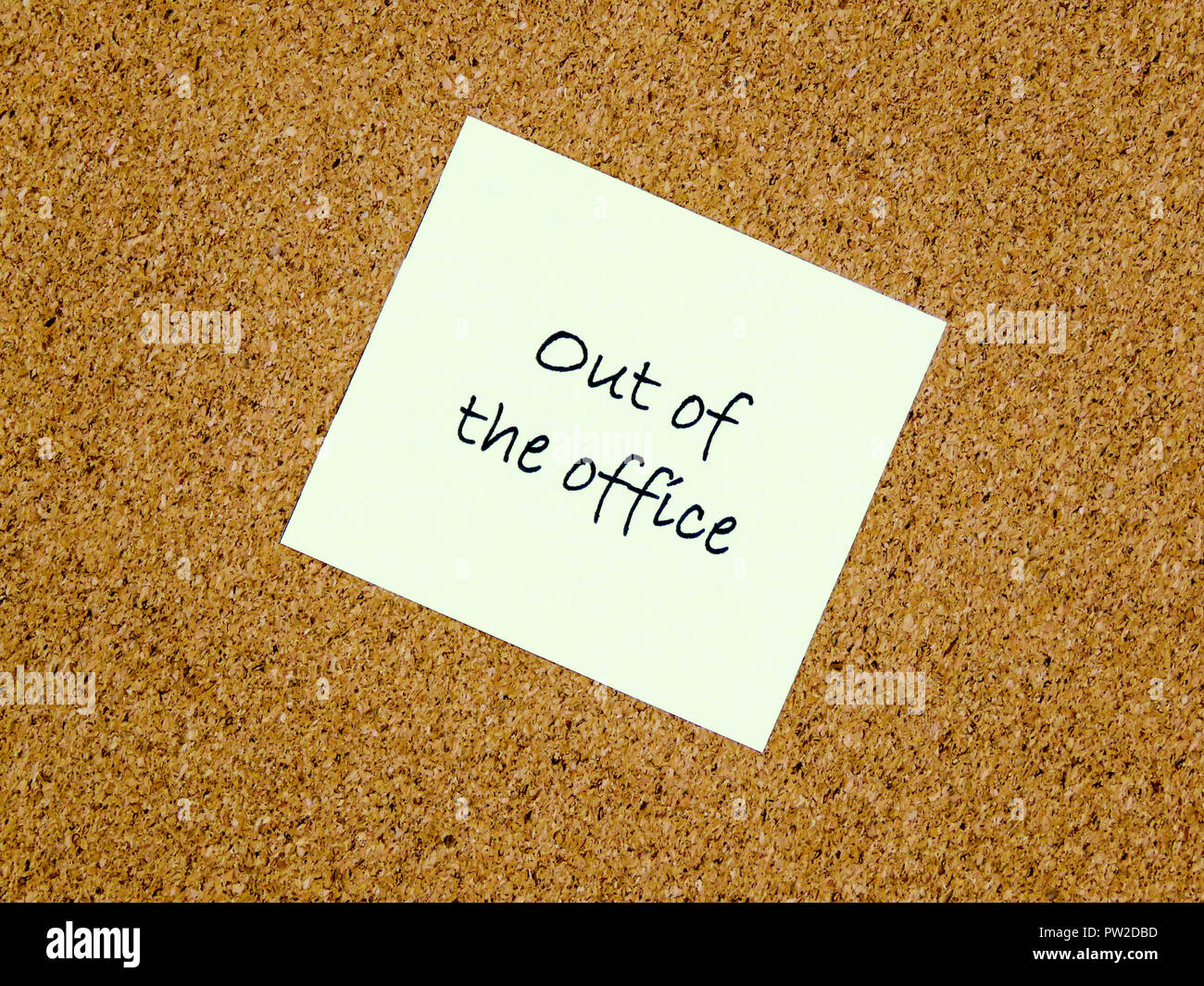 A yellow sticky note with out of office written on it on a cork board ...