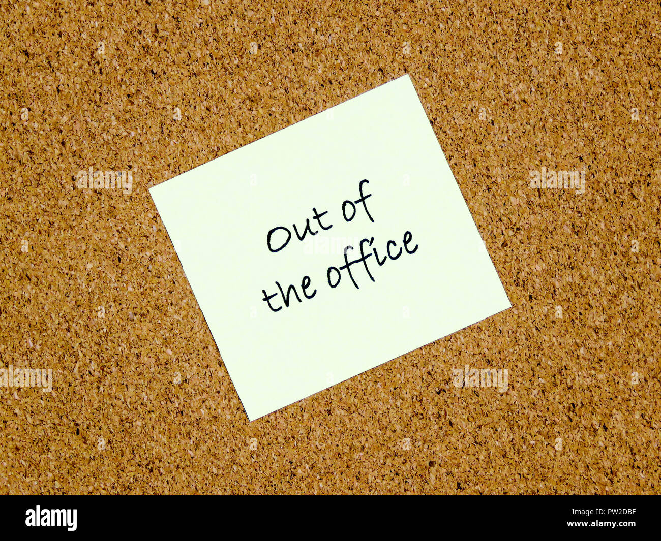 A yellow sticky note with out of office written on it on a cork board ...