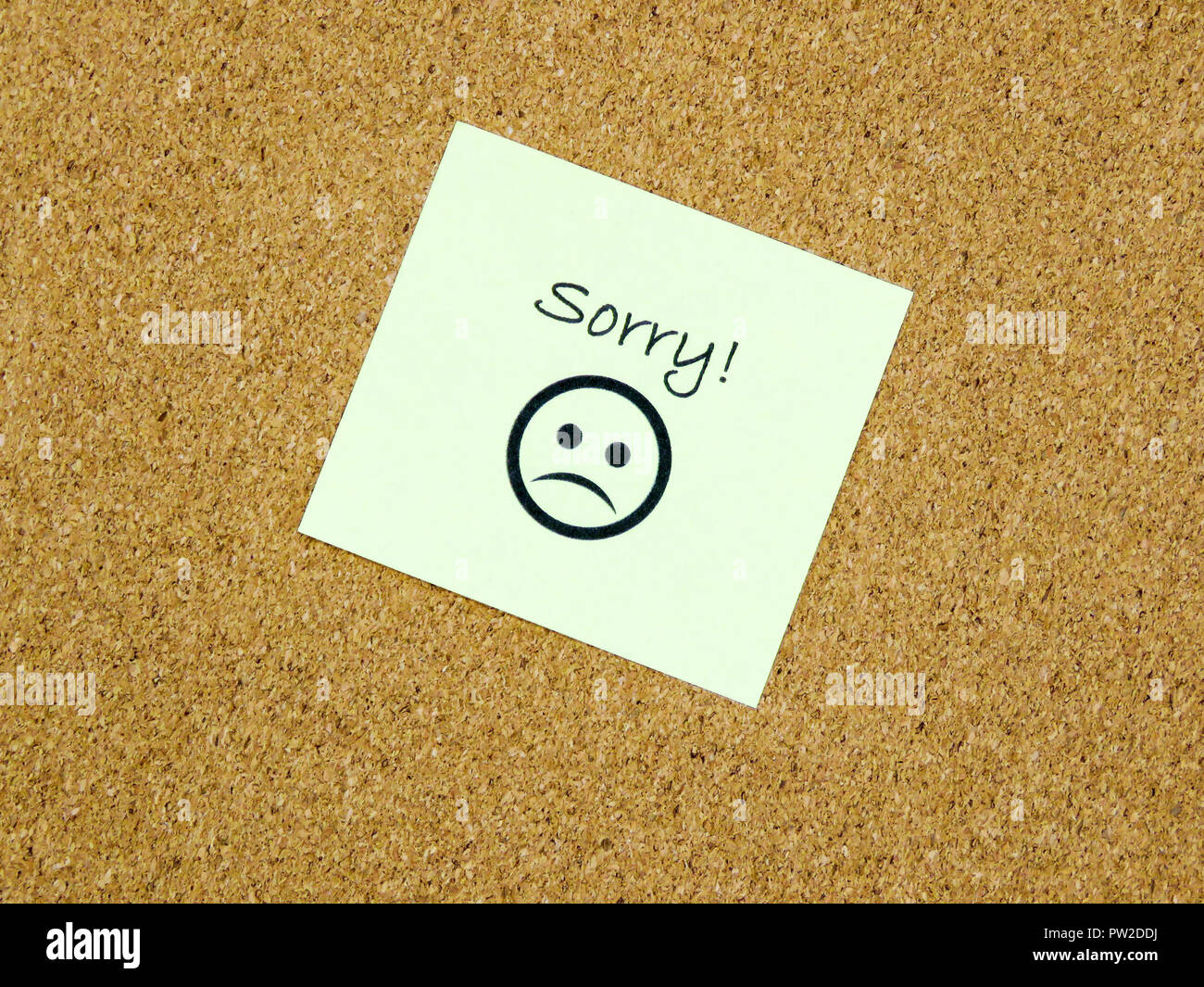 A yellow sticky note with sorry written on it on a cork board ...