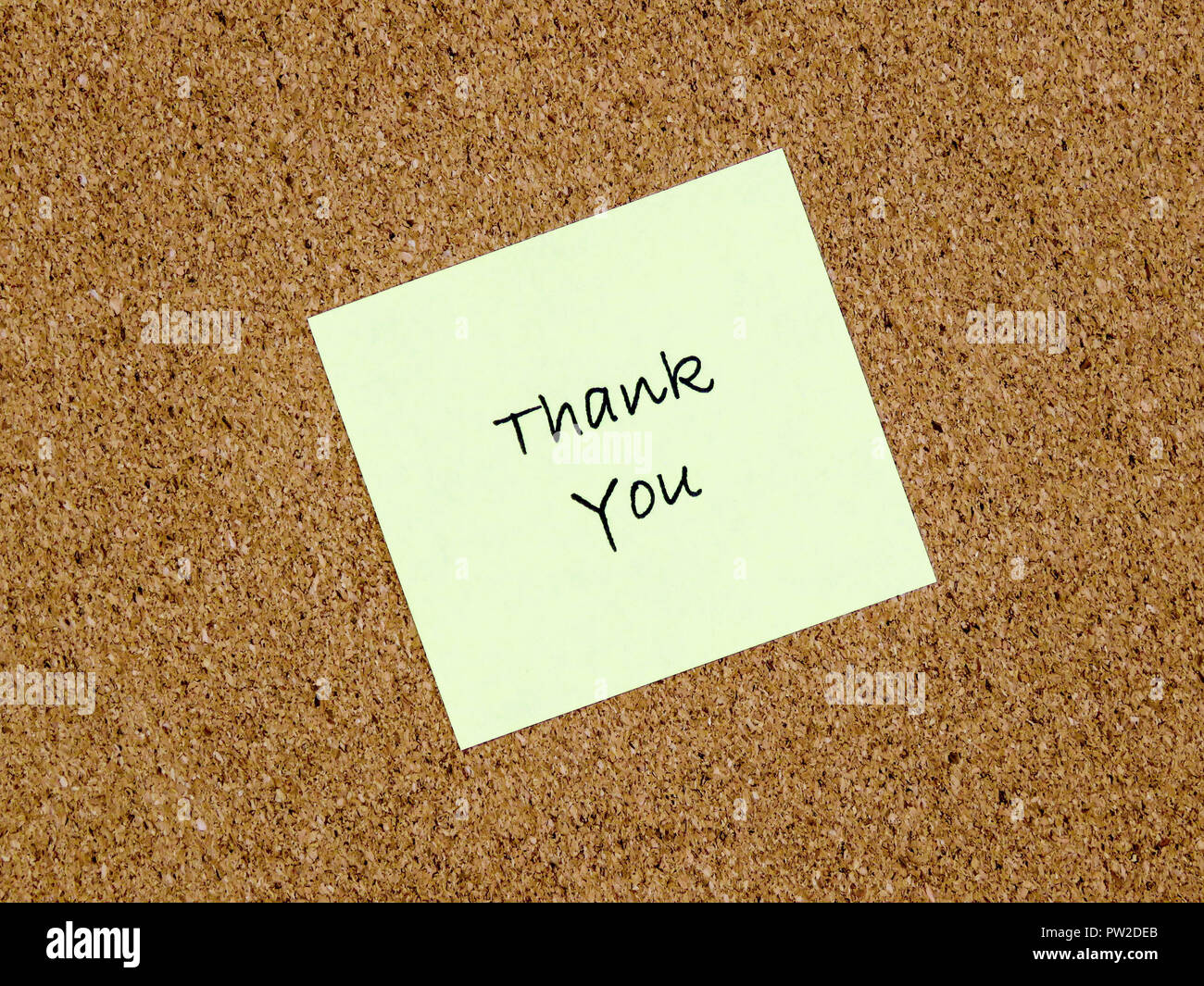 A yellow sticky note with thank you written on it on a cork board ...