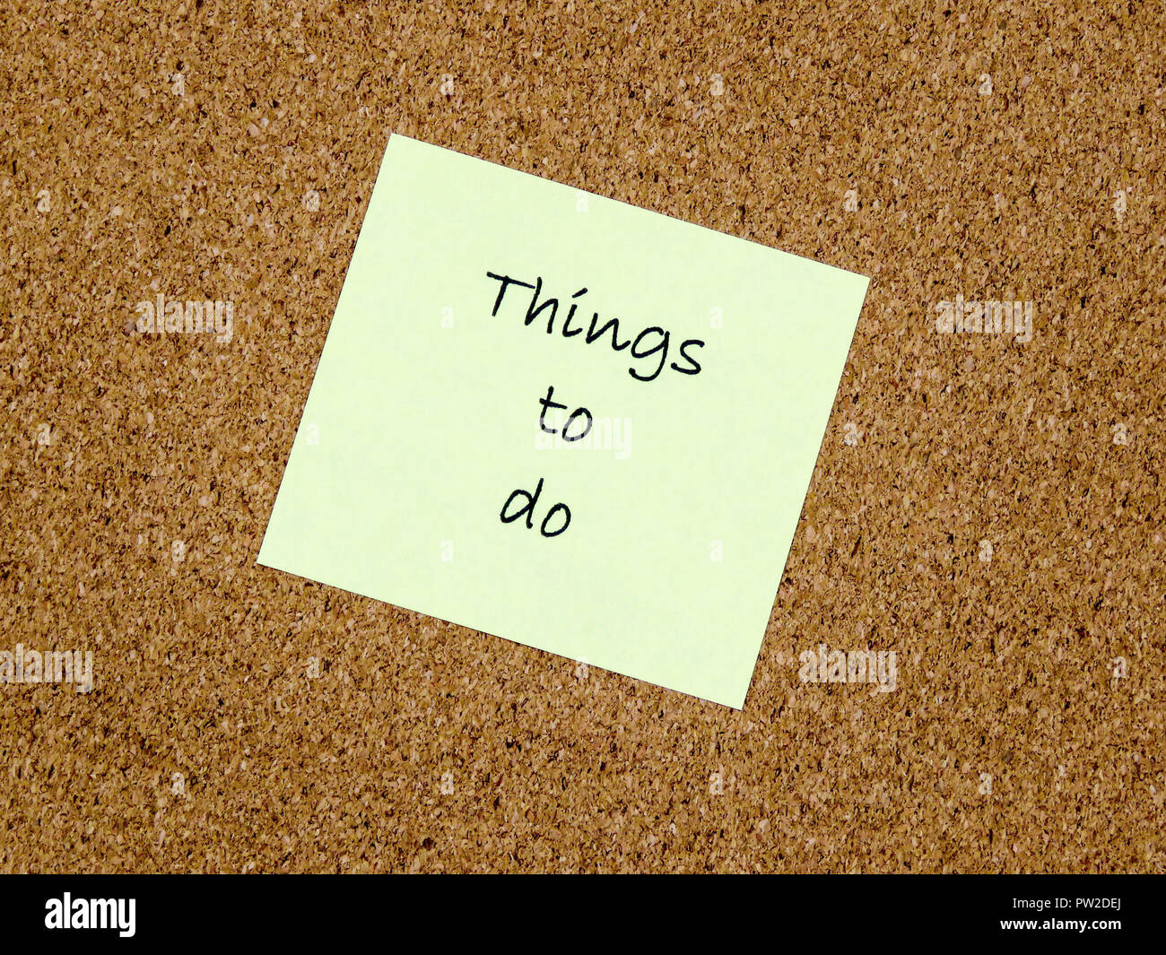 A yellow sticky note with things to do written on it on a cork board ...