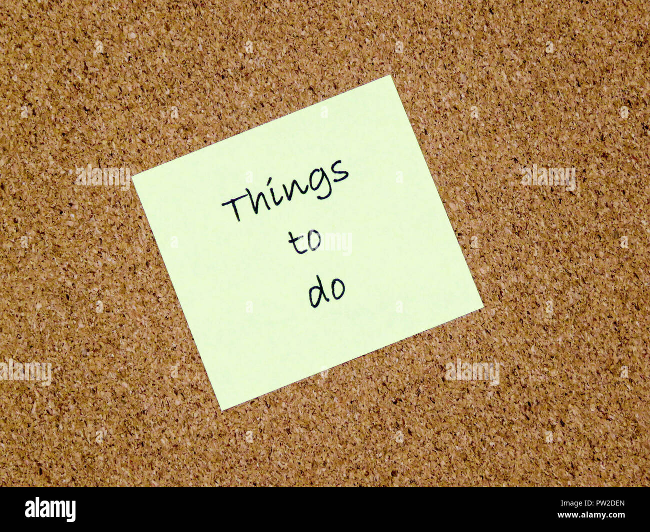 A yellow sticky note with things to do written on it on a cork board ...