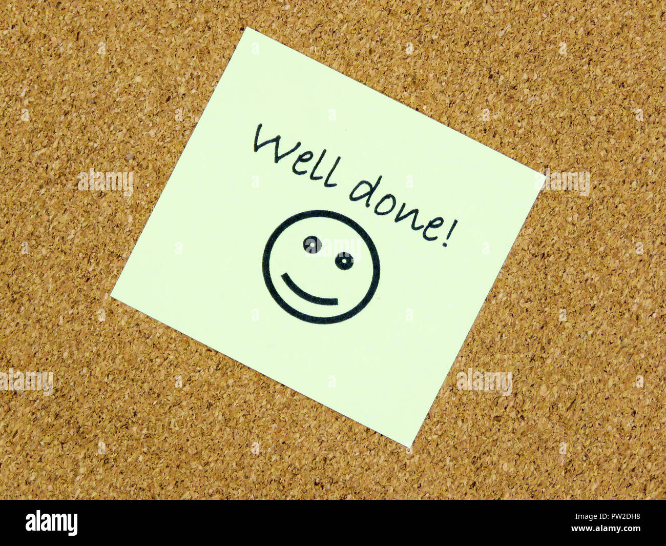 A yellow sticky note with well done written on it on a cork board ...