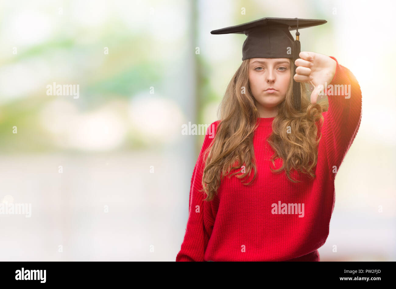 Young blonde woman wearing graduation cap with angry face, negative ...