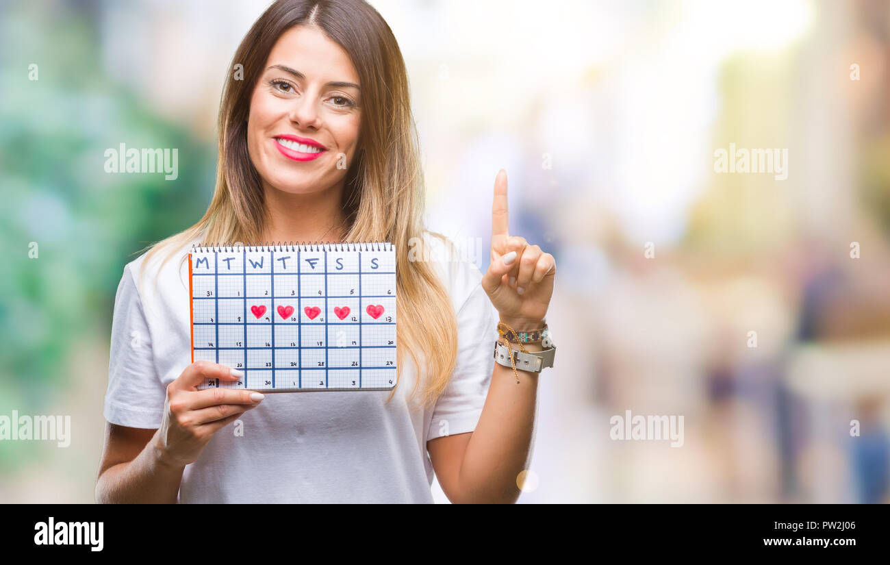 Young beautiful woman holding menstruation calendar over isolated ...