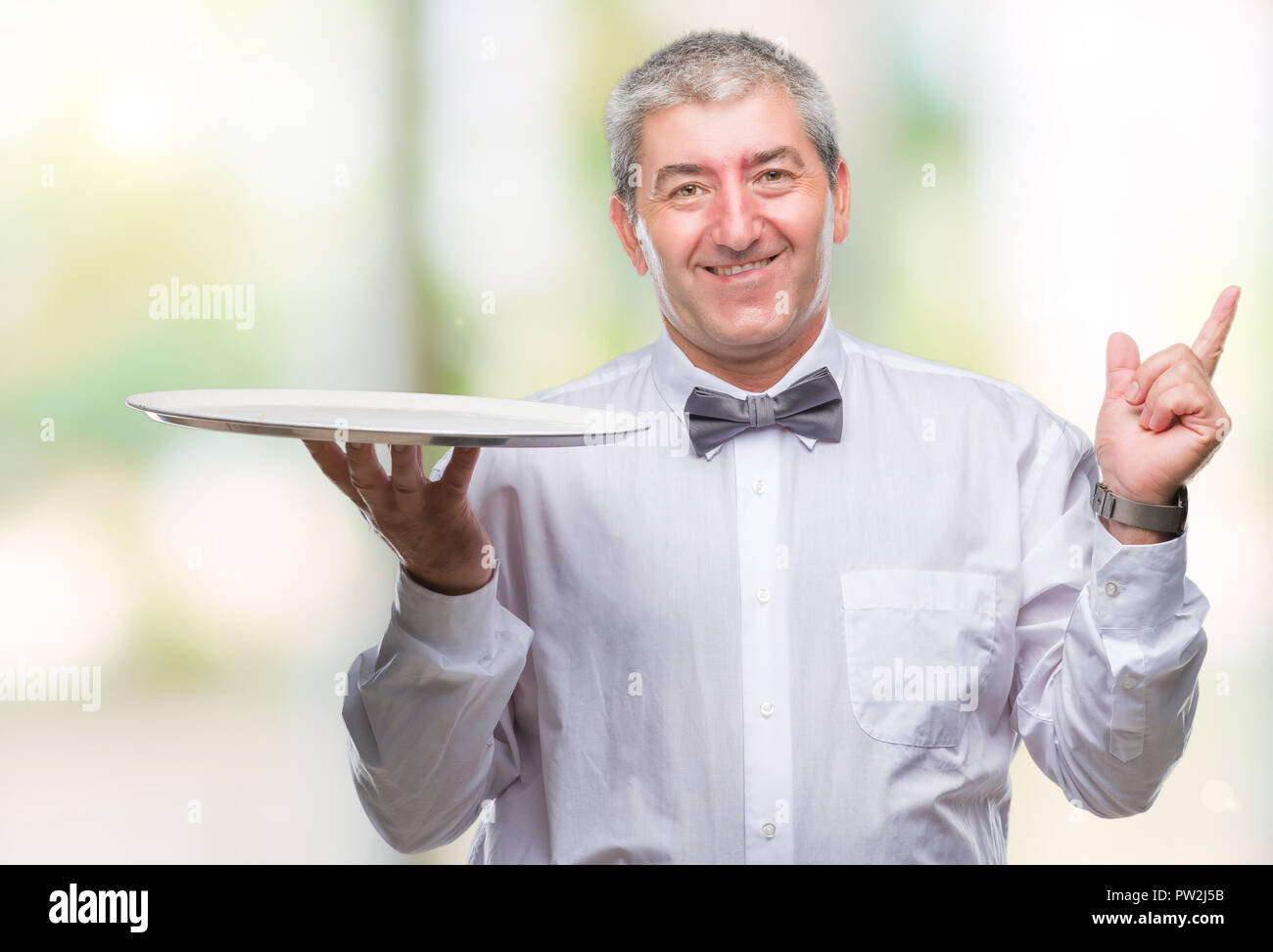 Handsome senior waiter man holding silver tray over isolated background ...