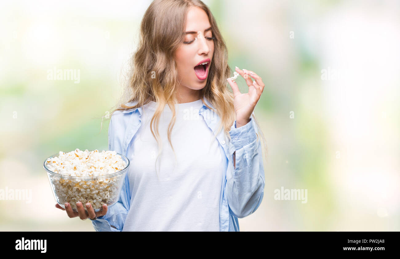 Beautiful young blonde woman eating popcorn over isolated background ...
