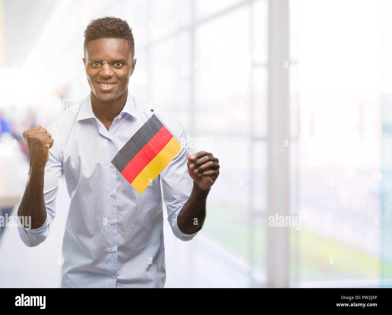 Young african american man holding german flag screaming proud and ...