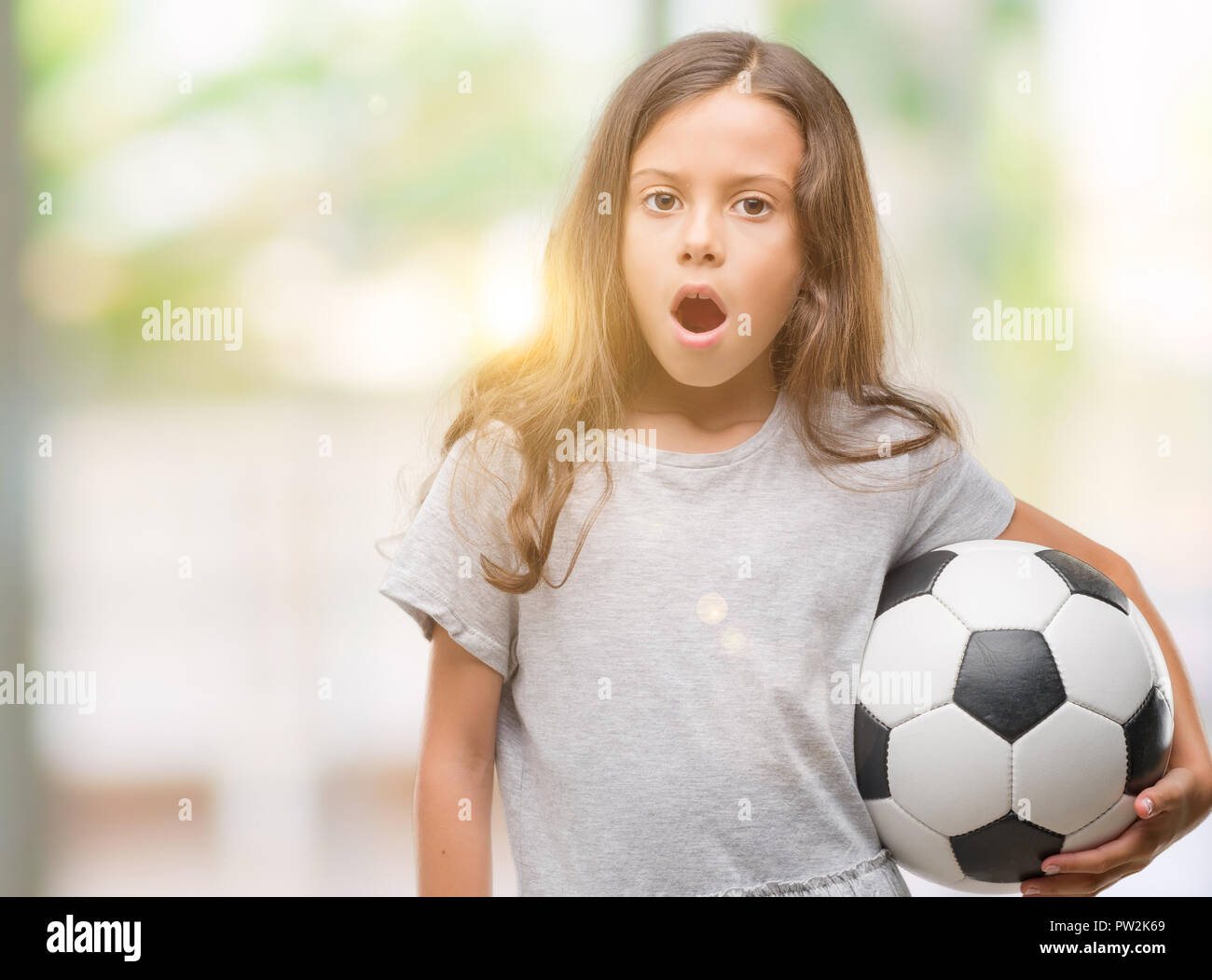 Brunette hispanic girl holding soccer football ball scared in shock ...