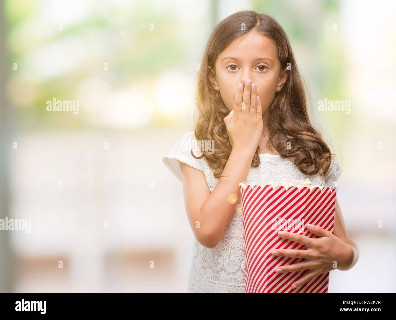 Brunette hispanic girl eating popcorn cover mouth with hand shocked ...