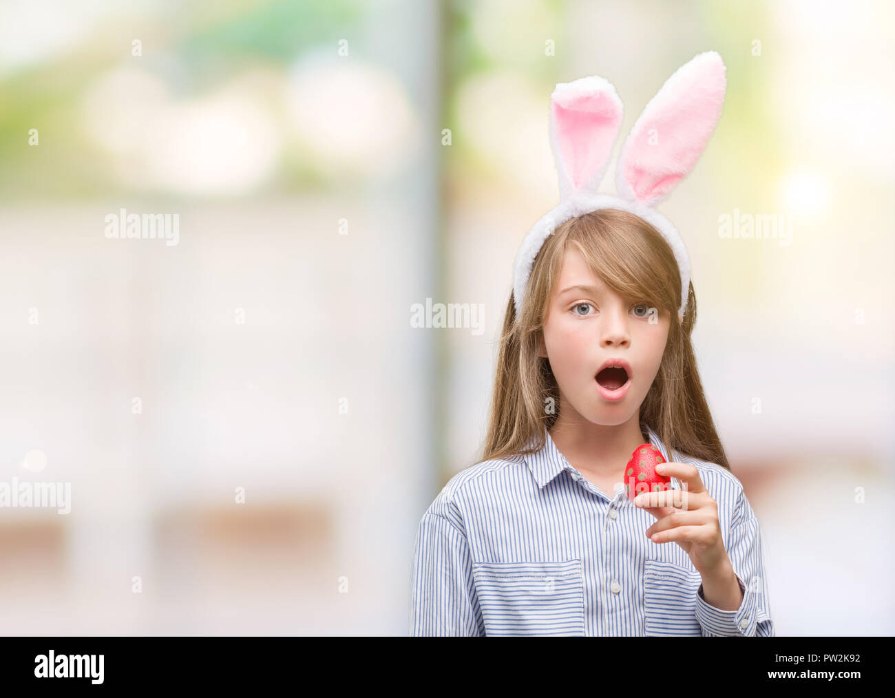 Young blonde child wearing easter bunny ears scared in shock with a ...