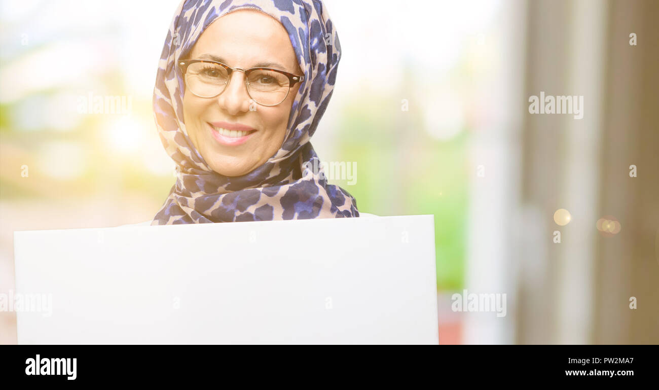 Middle age muslim arab woman wearing hijab holding blank advertising ...