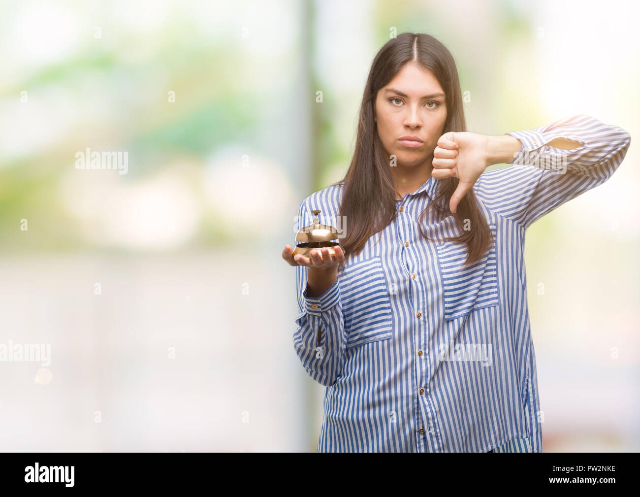 Young beautiful hispanic holding hotel ring bell with angry face ...