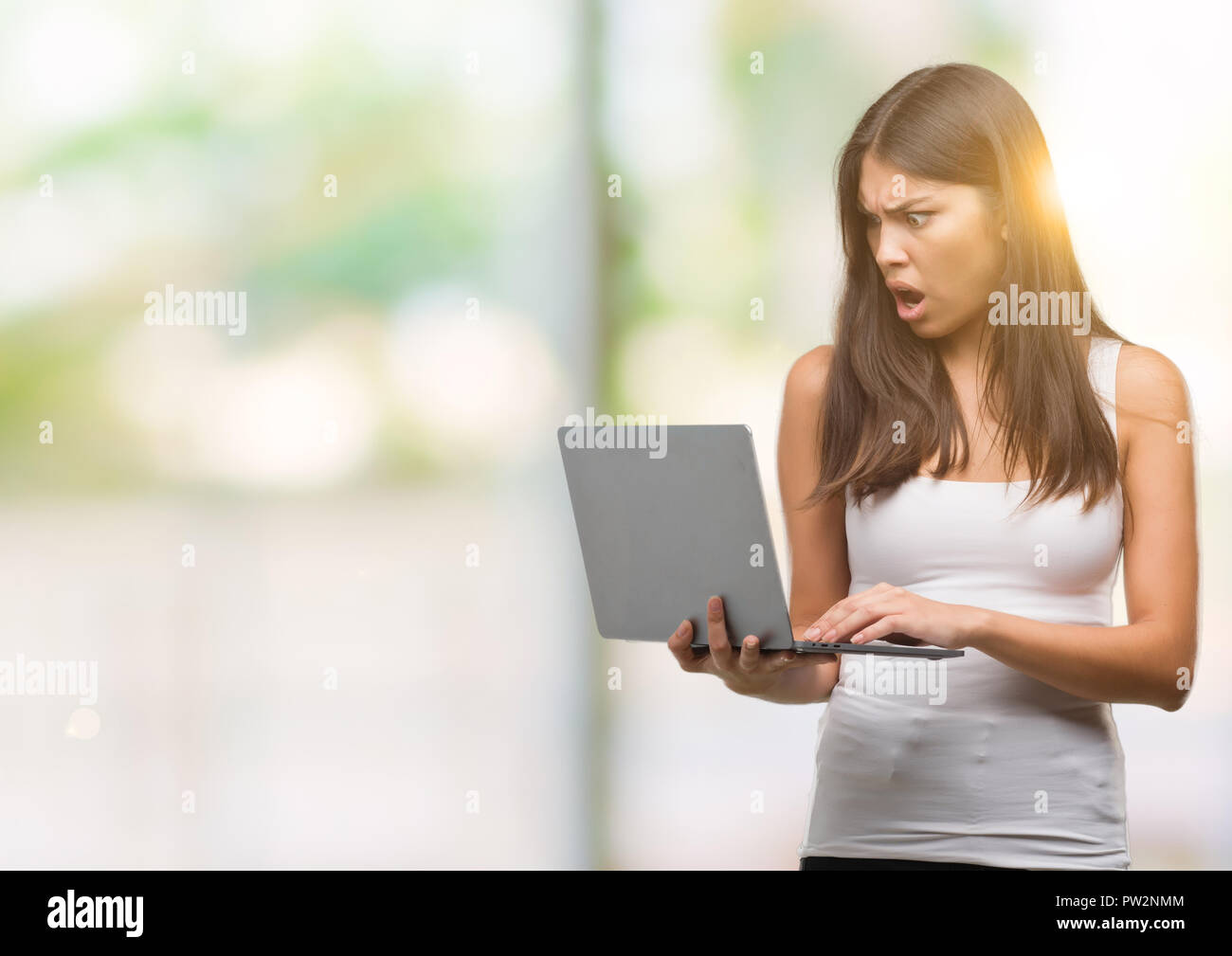 Young hispanic woman using computer laptop scared in shock with a ...