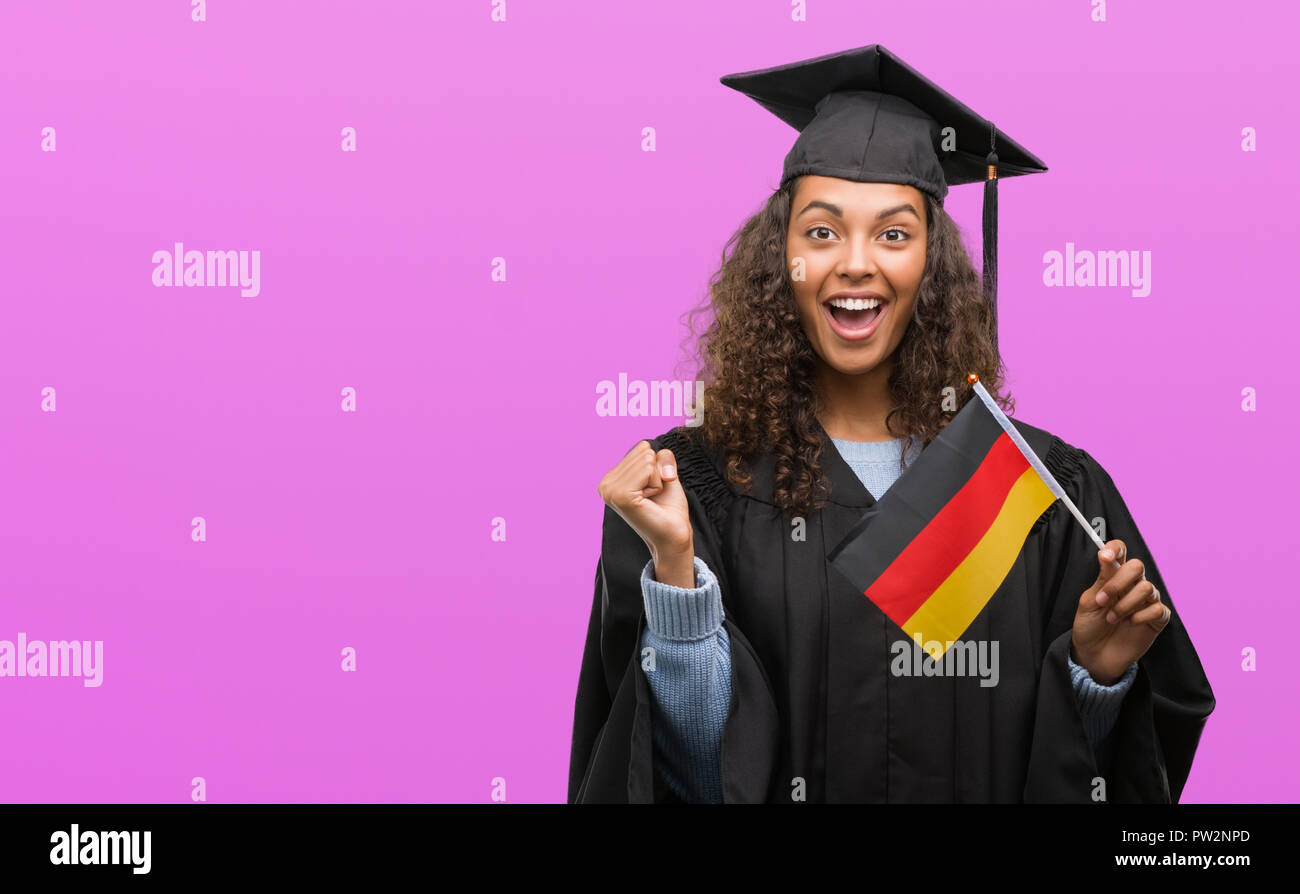 Young hispanic woman wearing graduation uniform holding flag of Germany ...