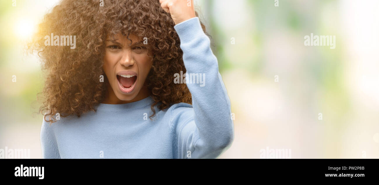 African american woman wearing a sweater angry and mad raising fist ...