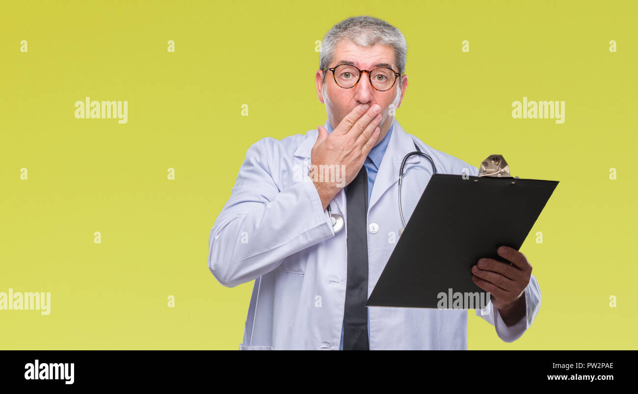 Handsome senior doctor man holding clipboard over isolated background ...