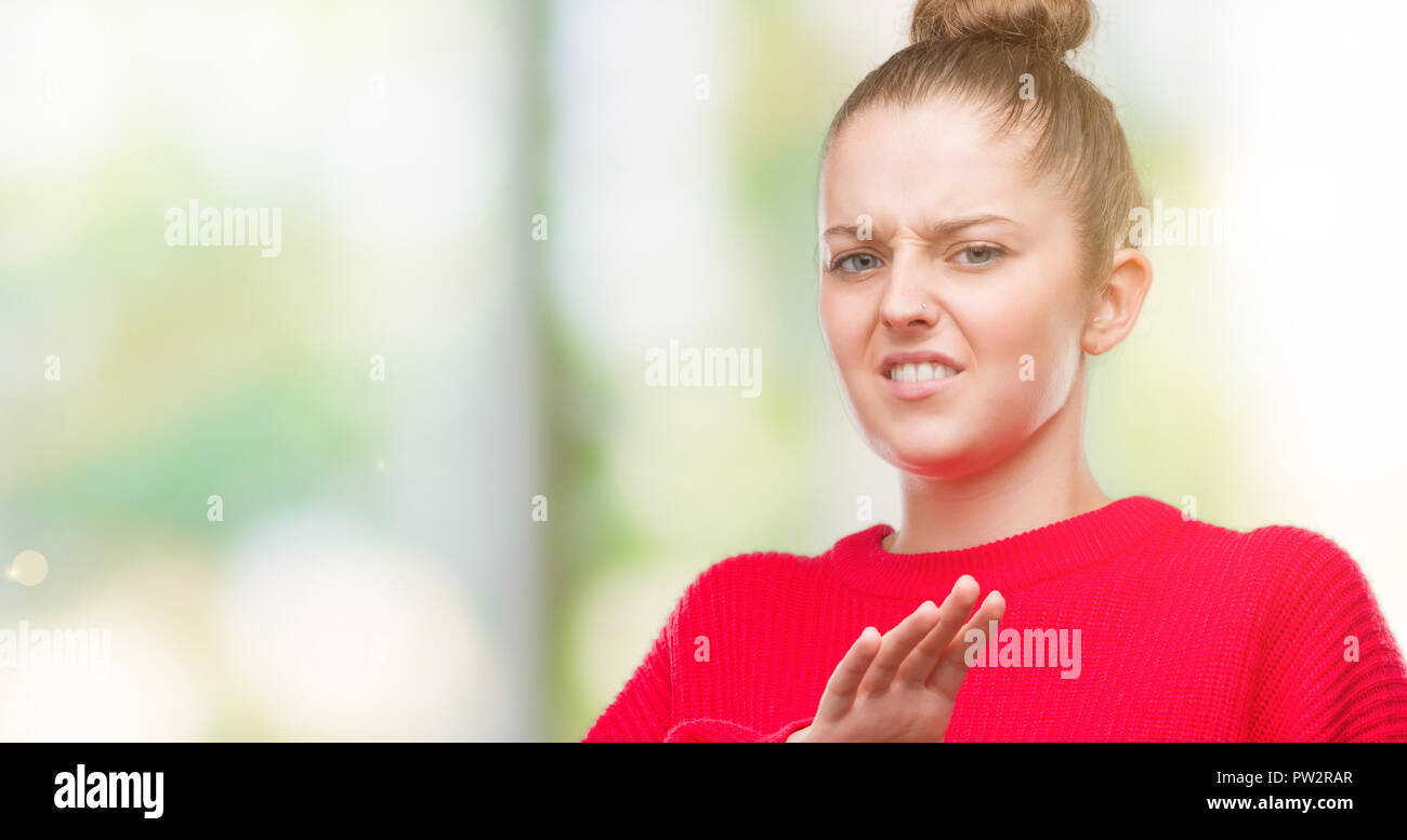 Young blonde woman wearing bun and red sweater disgusted expression ...
