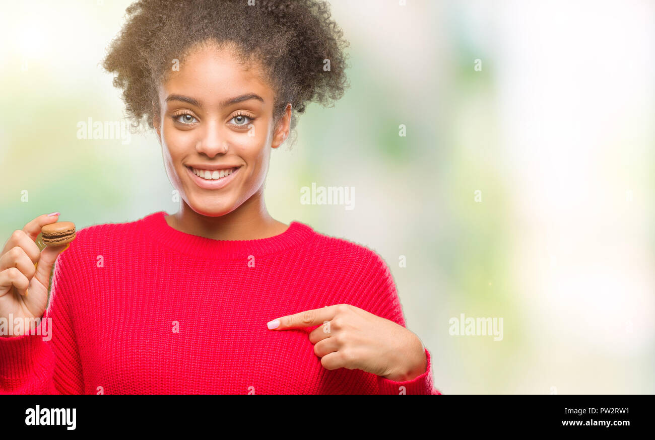 Young afro american woman eating chocolate macaron over isolated ...