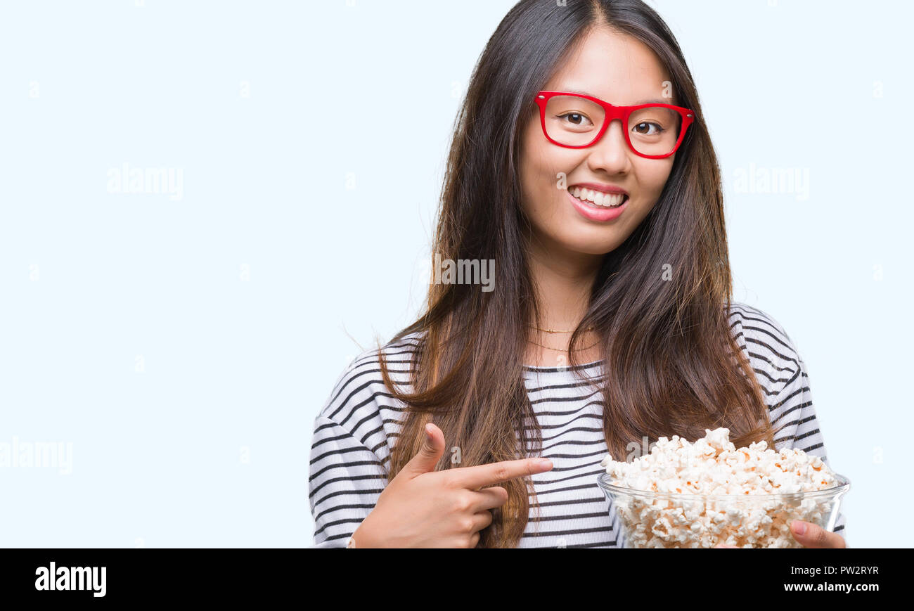 Young asian woman eating popcorn over isolated background very happy ...