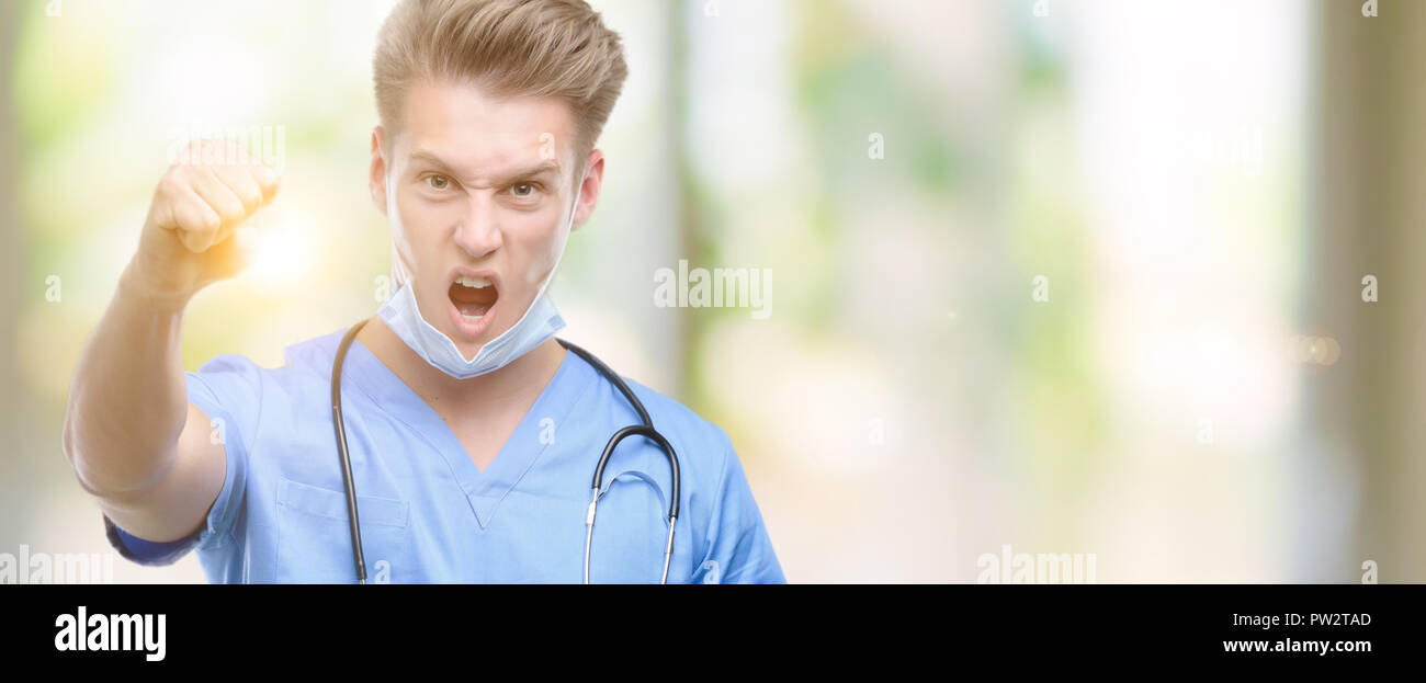 Young handsome blond doctor annoyed and frustrated shouting with anger ...