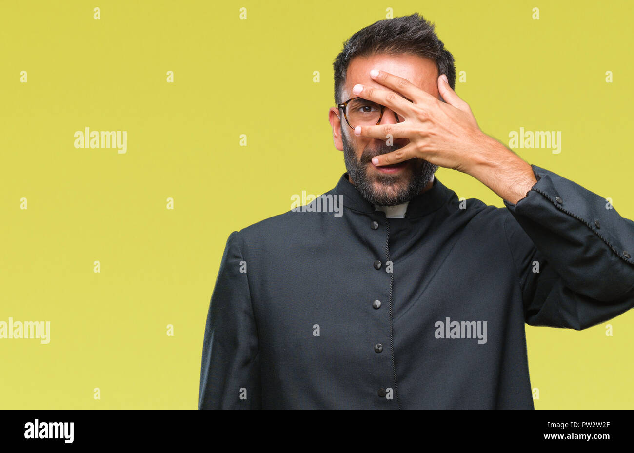Adult hispanic catholic priest man over isolated background peeking in ...