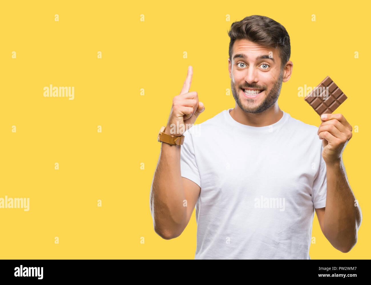 Young handsome man eating chocolate bar over isolated background ...