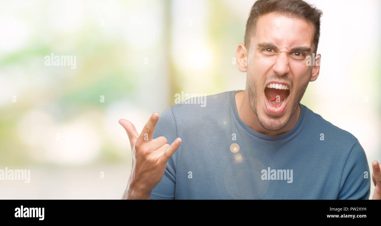 Handsome young casual man shouting with crazy expression doing rock ...