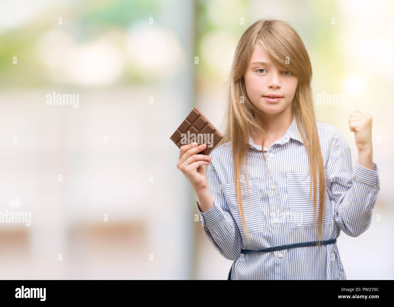 Young blonde child holding chocolate bar screaming proud and ...