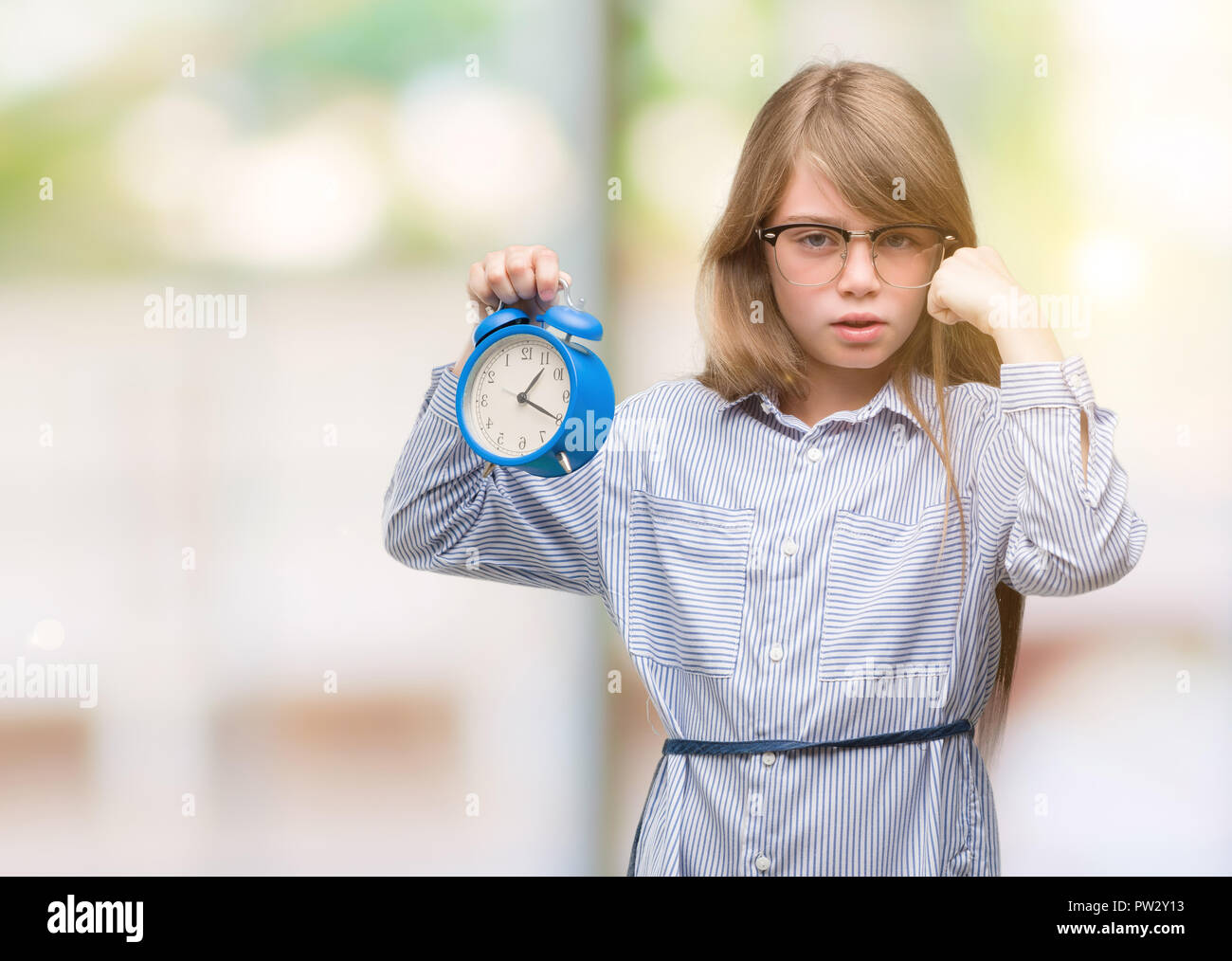 Young blonde child holding alarm clock annoyed and frustrated shouting ...