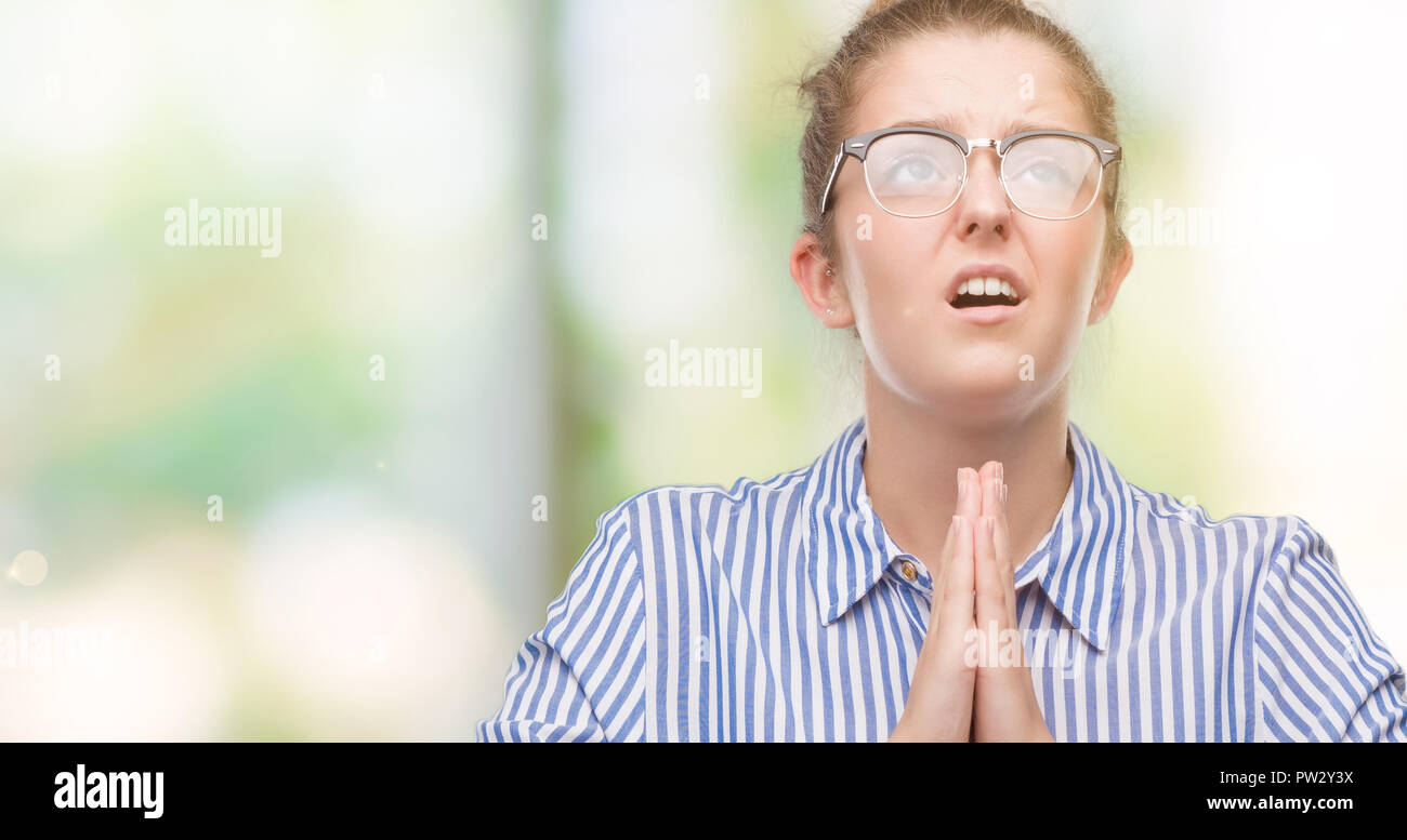 Young blonde business woman begging and praying with hands together ...