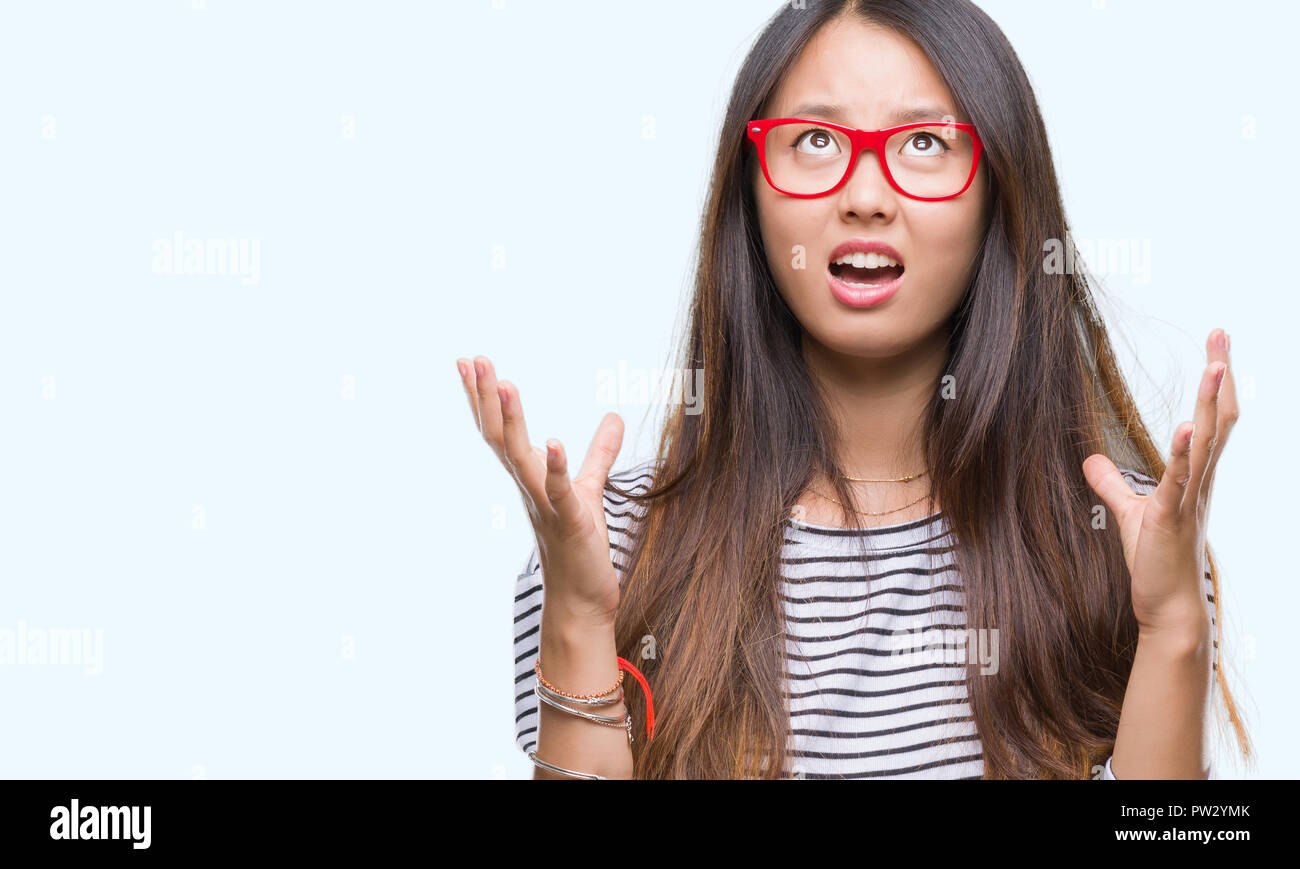 Young asian woman wearing glasses over isolated background crazy and ...