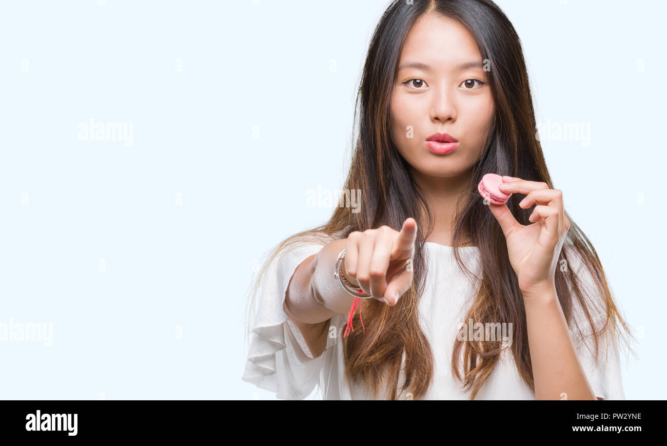 Young asian woman eating pink macaron sweet over isolated background ...