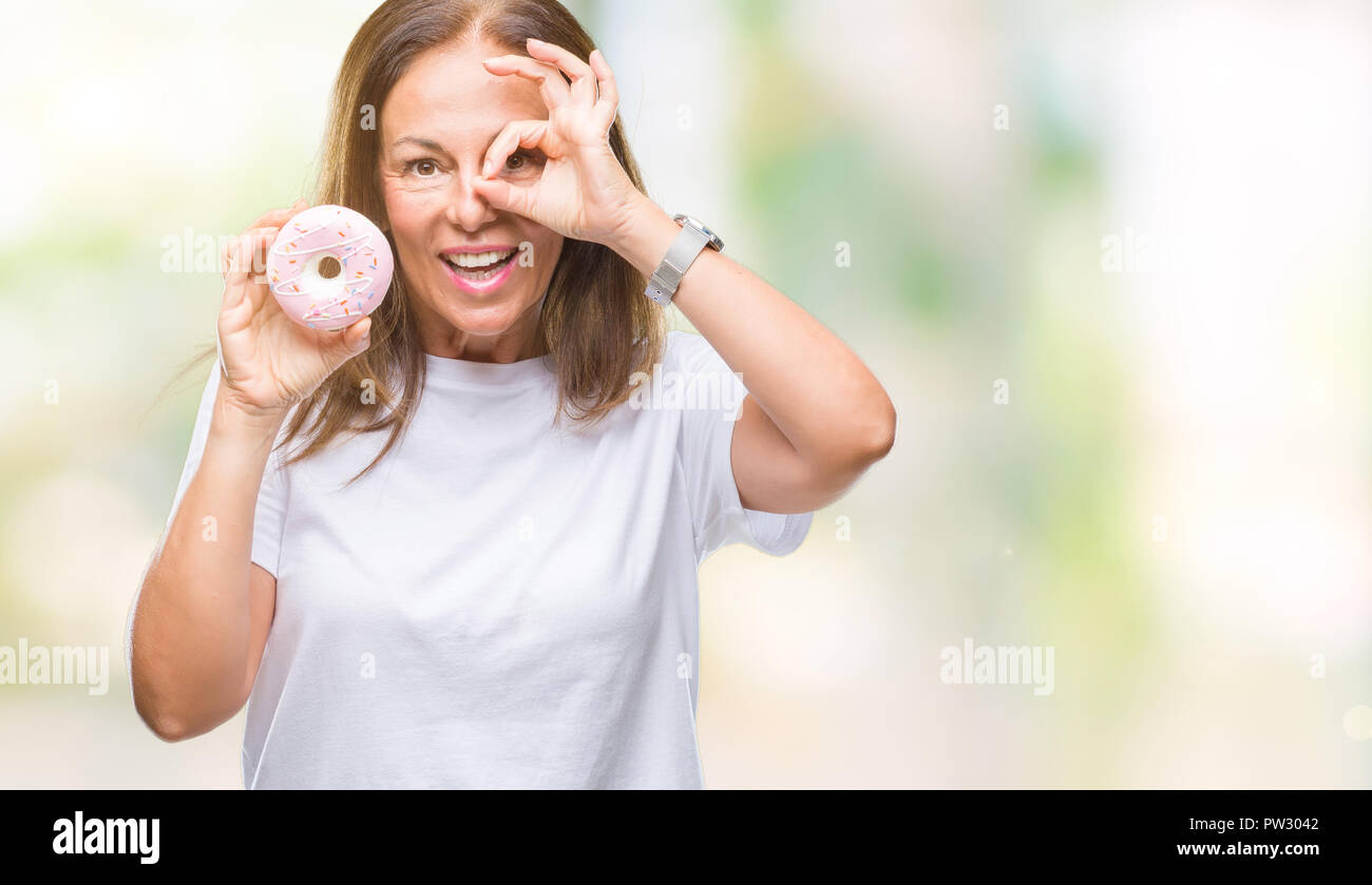 Middle age hispanic woman eating pink donut over isolated background ...
