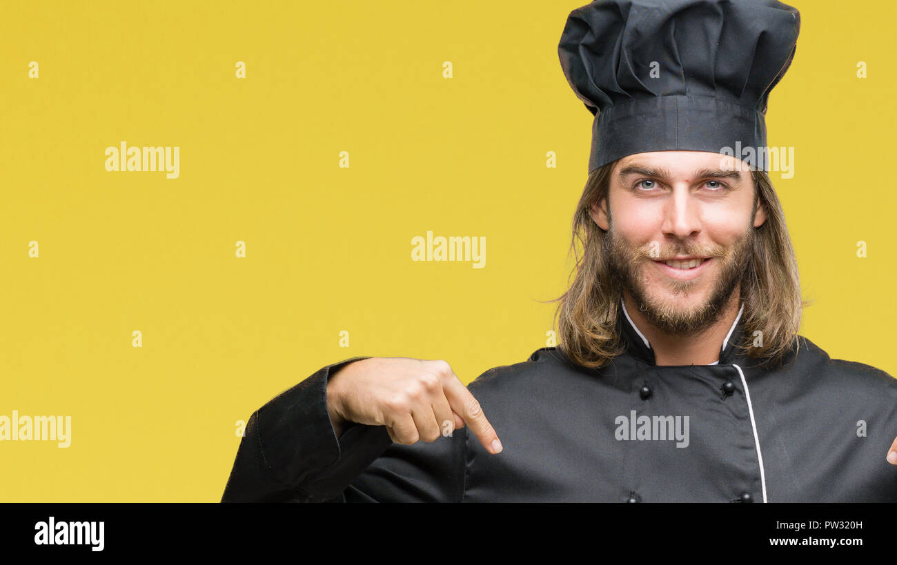 Young handsome cook man with long hair over isolated background looking ...