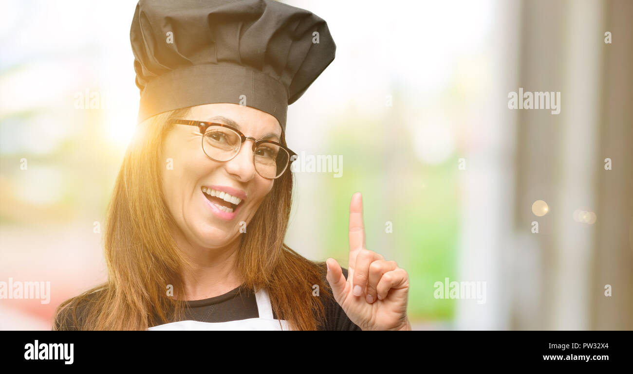 Middle age cook woman wearing chef apron pointing away side with finger ...