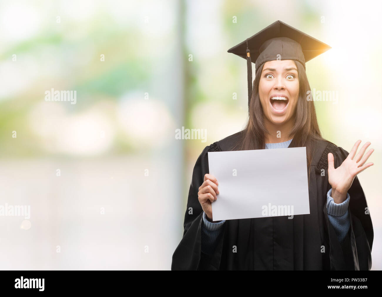 Young hispanic woman wearing graduated uniform holding diploma paper ...