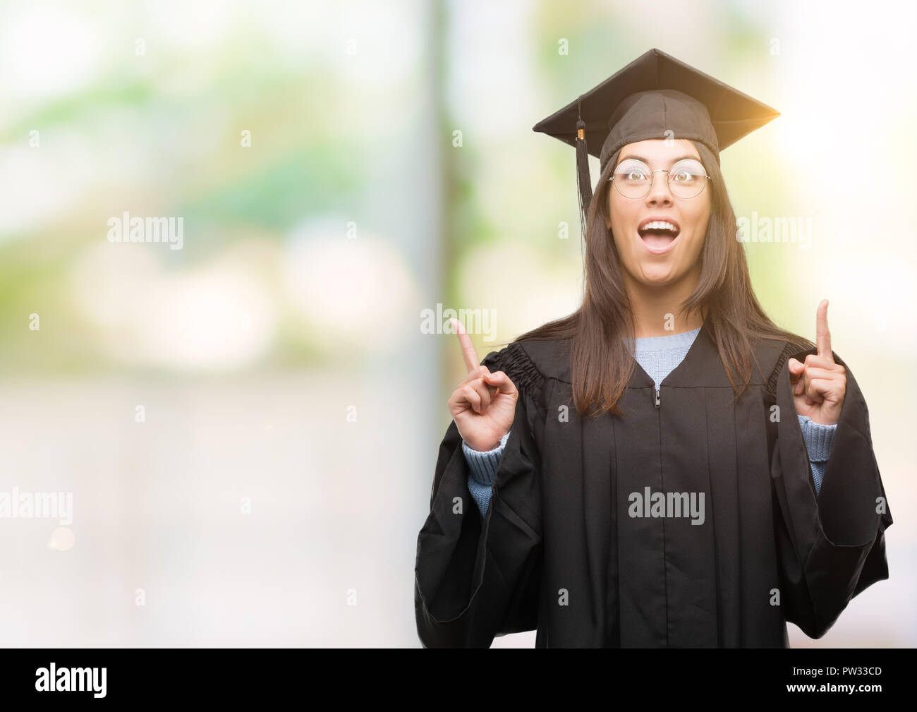 Young hispanic woman wearing graduated cap and uniform amazed and ...