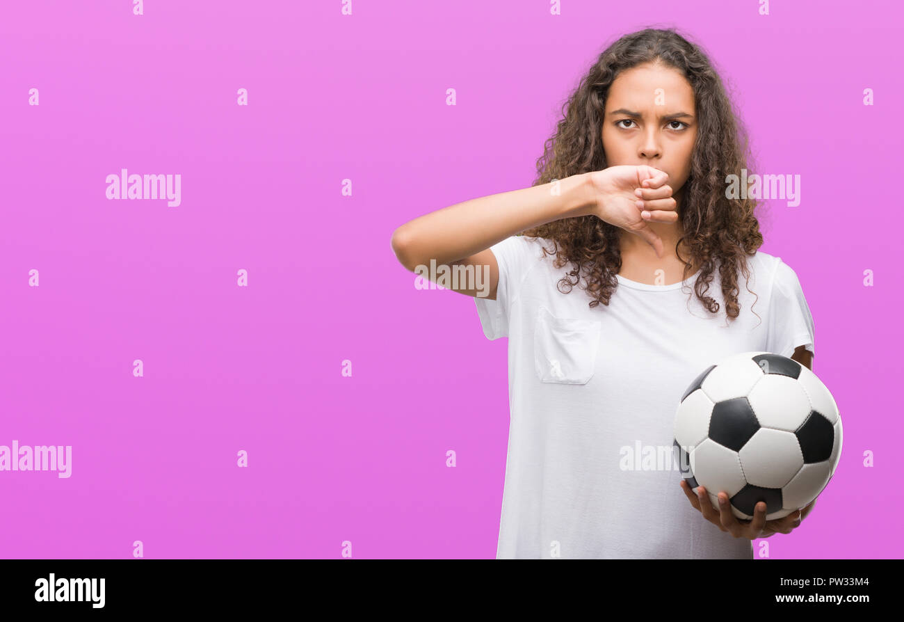 Young hispanic woman holding soccer football ball with angry face ...